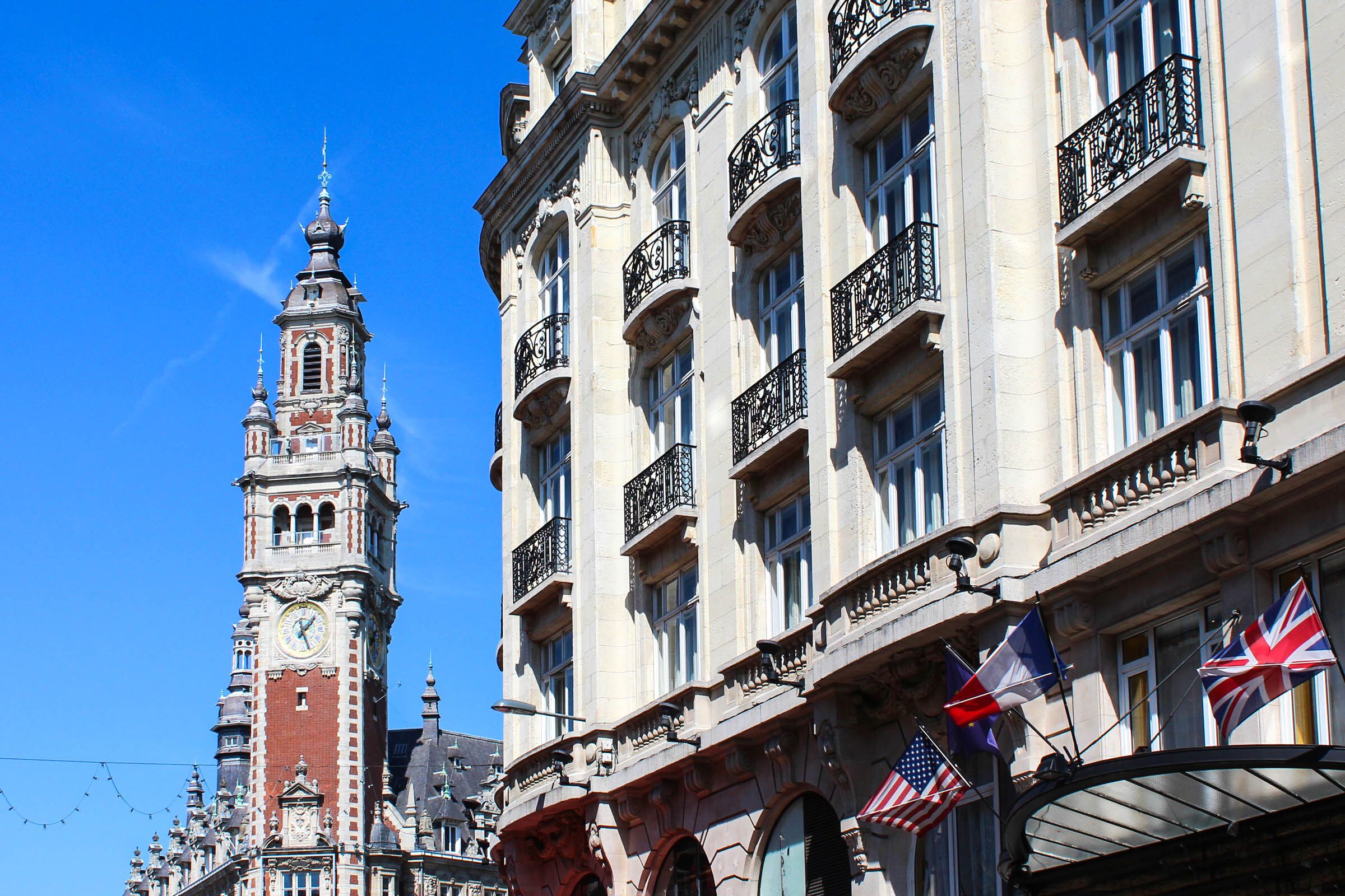 Um edifício histórico com arquitetura elaborada, uma torre do relógio e várias bandeiras, incluindo a bandeira britânica.