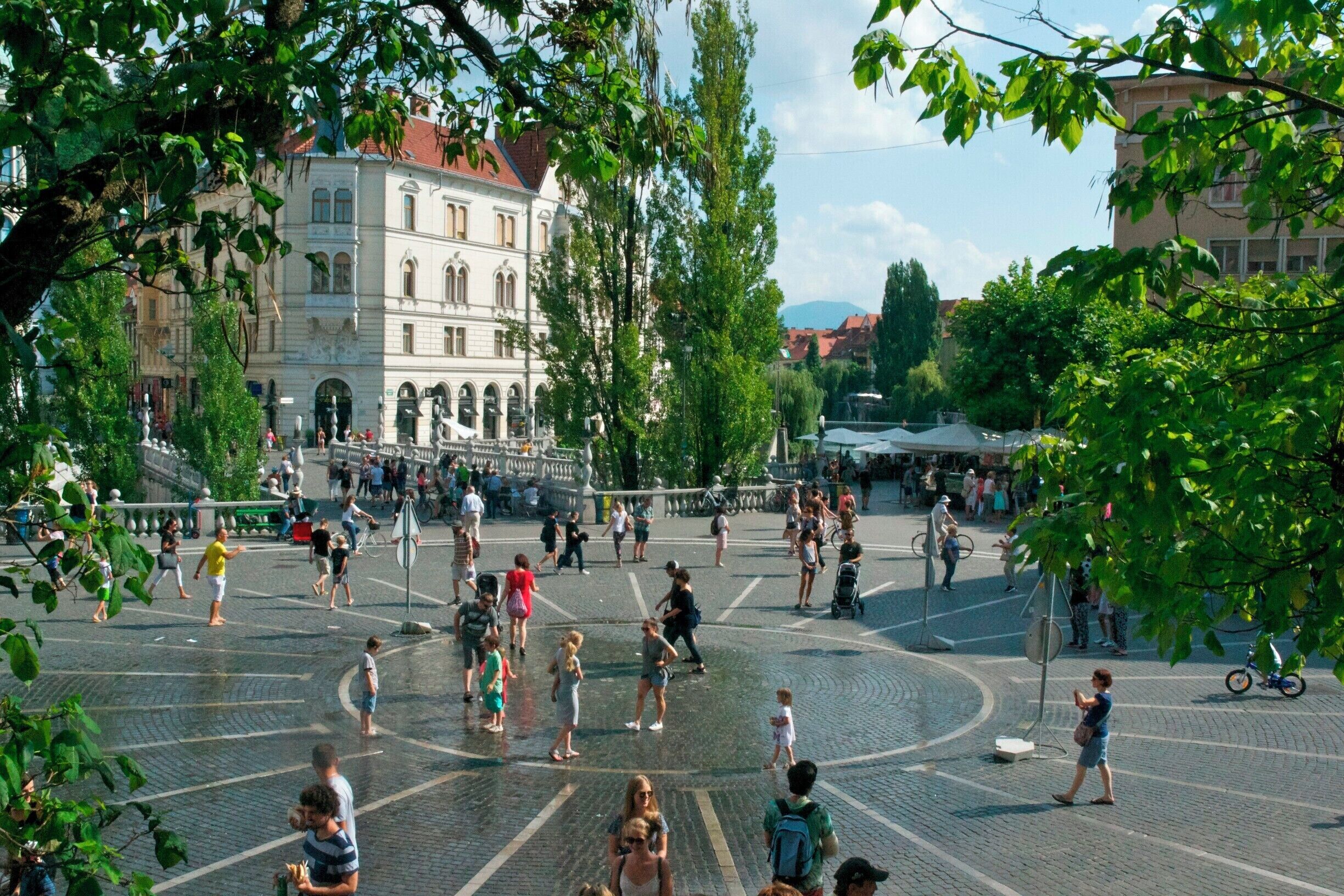 Uma praça pública com calçamento de pedra, rodeada por árvores e edifícios.
