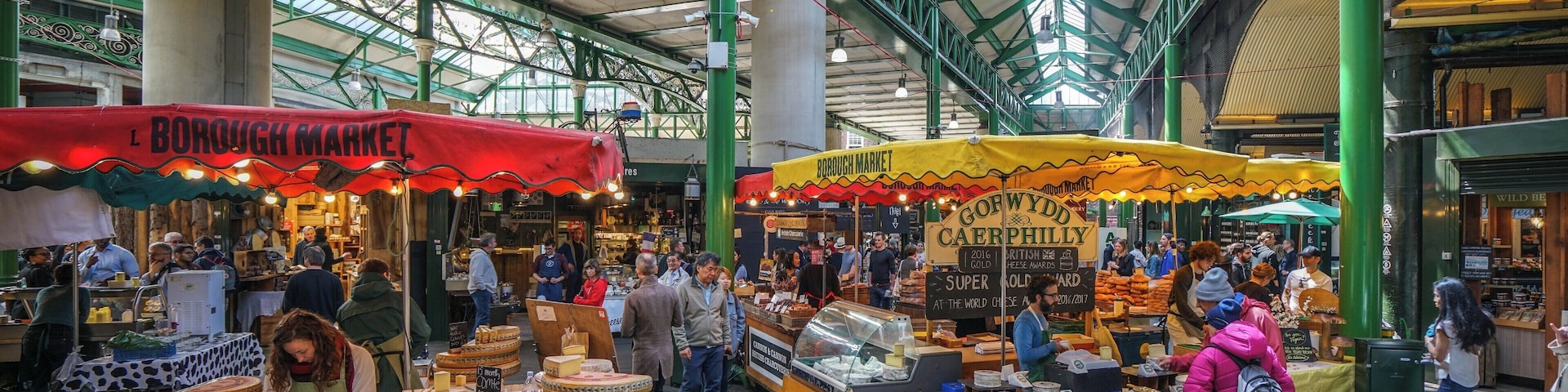 Um mercado interno movimentado com diversos quiosques, incluindo um de queijos e outro de produtos frescos.