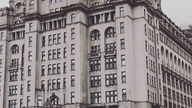 Um edifício histórico com arquitetura ornamentada, incluindo uma torre do relógio e estátuas.