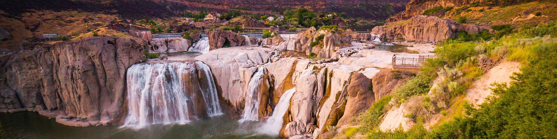 Uma cascata deságua em um rio, cercada por penhascos rochosos e vegetação.