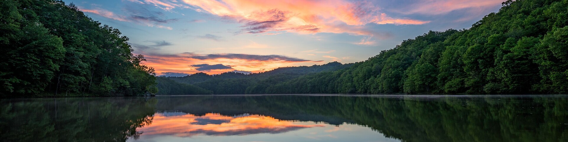 Um lago calmo refletindo o céu, rodeado por uma floresta densa.