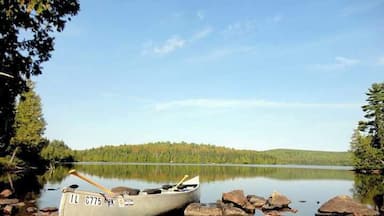Uma canoa com um remo numa margem rochosa perto de um lago calmo, rodeado de árvores.