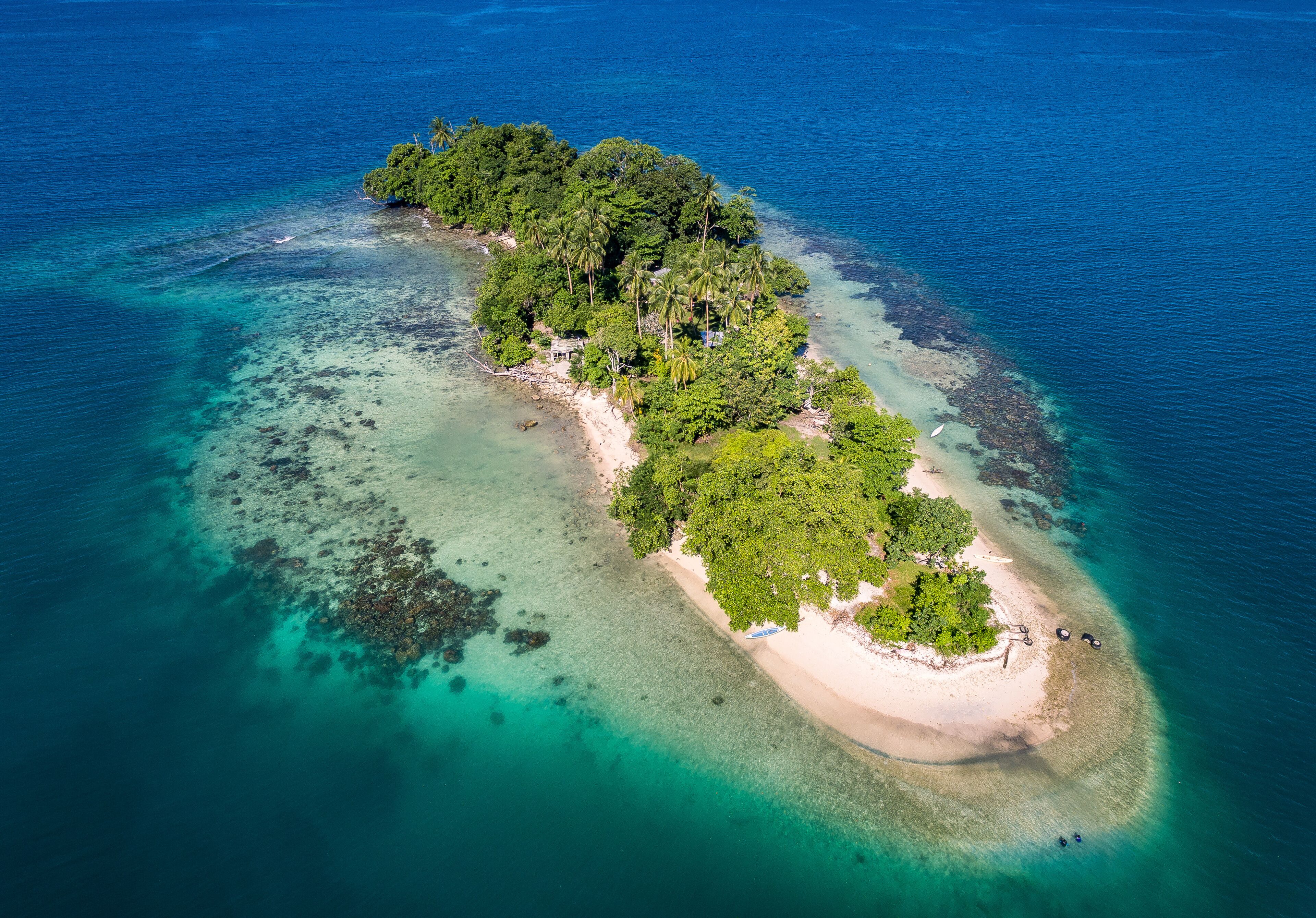 Vista aérea de uma ilha tropical com águas turquesa cristalinas, uma praia arenosa e vegetação verde exuberante.