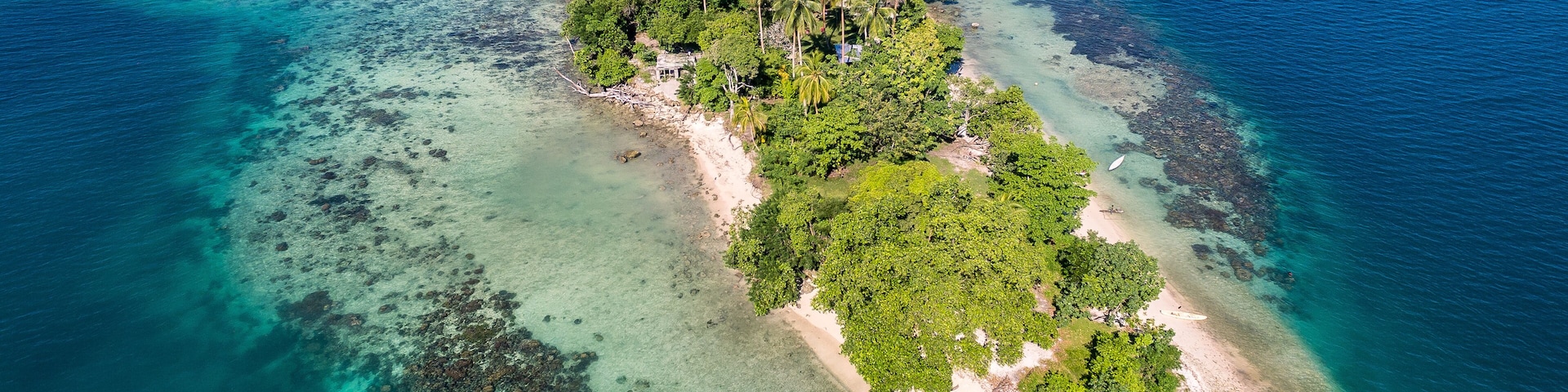 Vista aérea de uma ilha tropical com águas turquesa cristalinas, uma praia arenosa e vegetação verde exuberante.