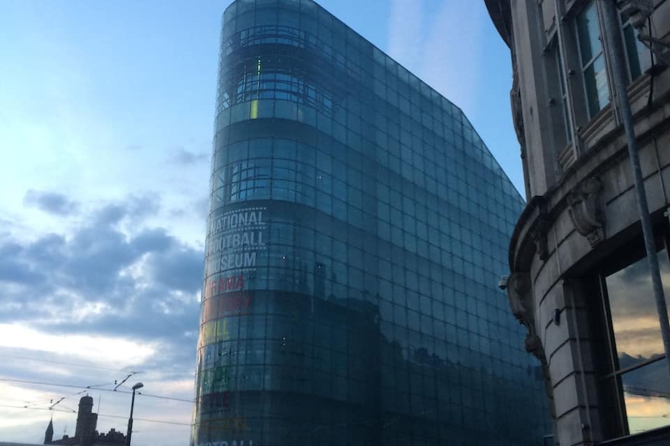 Um edifício moderno em vidro com a sinalização do Museu Nacional do Futebol e Teatro de Drama.
