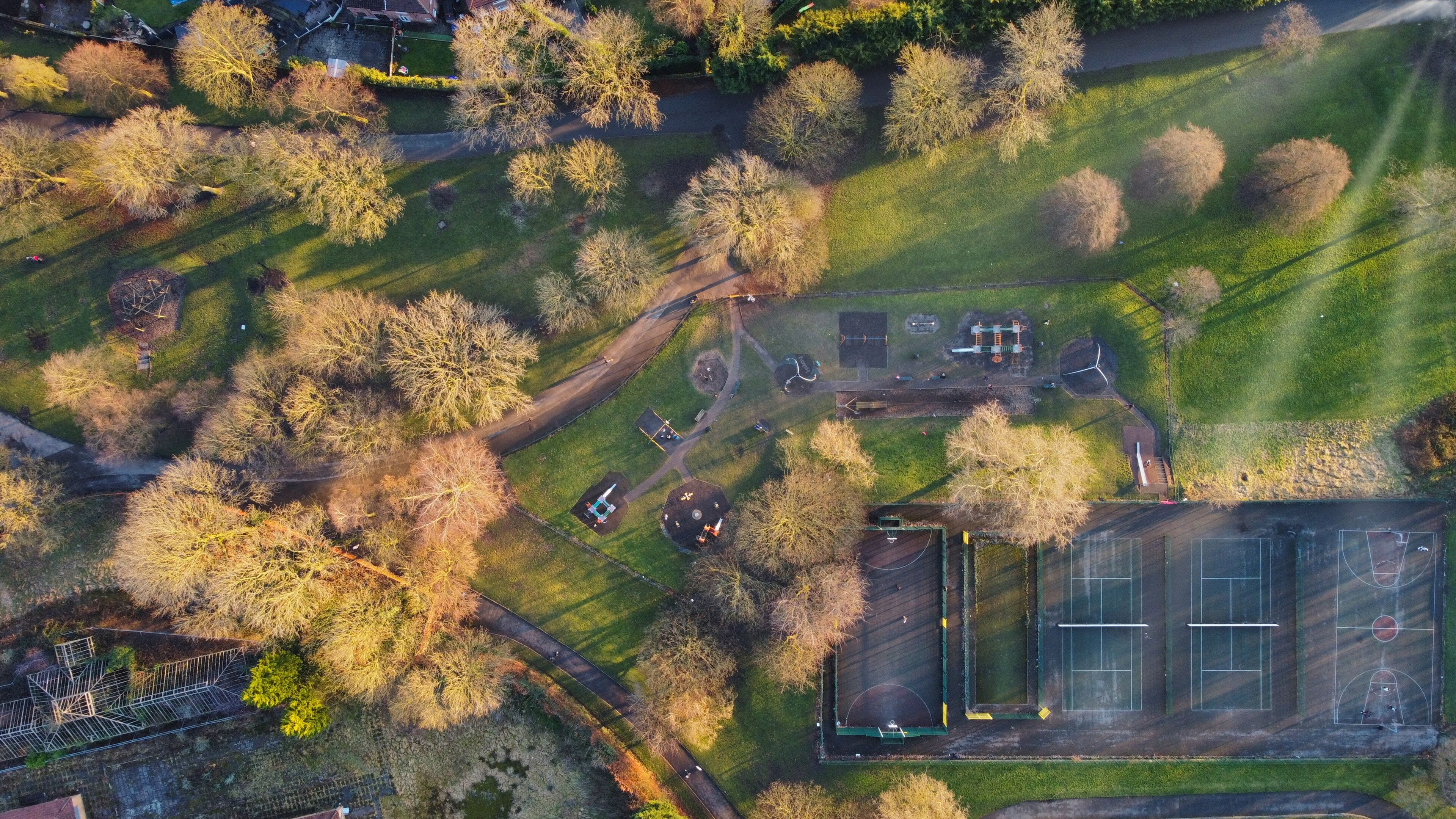 Vista aérea de um parque com árvores, um parquinho e uma quadra de basquete.