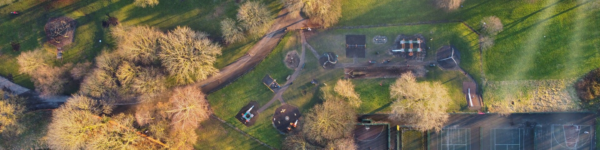 Vista aérea de um parque com árvores, um parquinho e uma quadra de basquete.