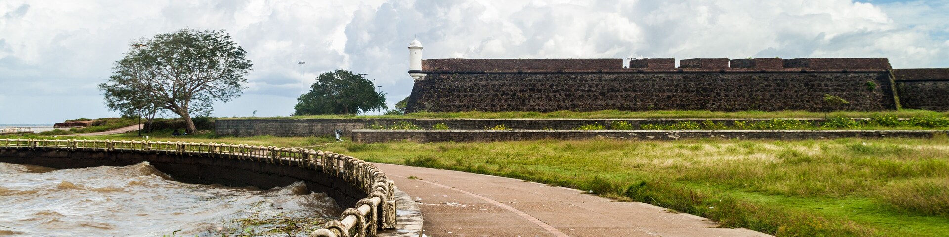 Um caminho costeiro com um muro de pedra e um farol ao fundo.