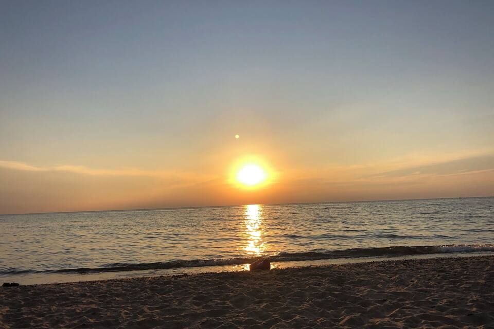 Um pôr do sol sobre uma praia, com o sol refletindo na água.