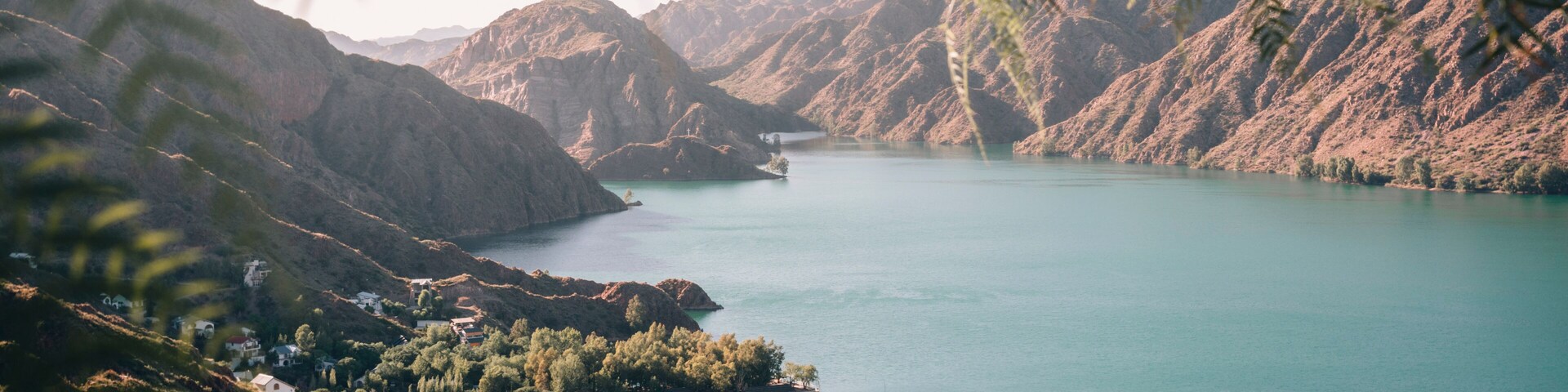 Paisagem montanhosa com um lago, rodeado por vegetação e edifícios pequenos.