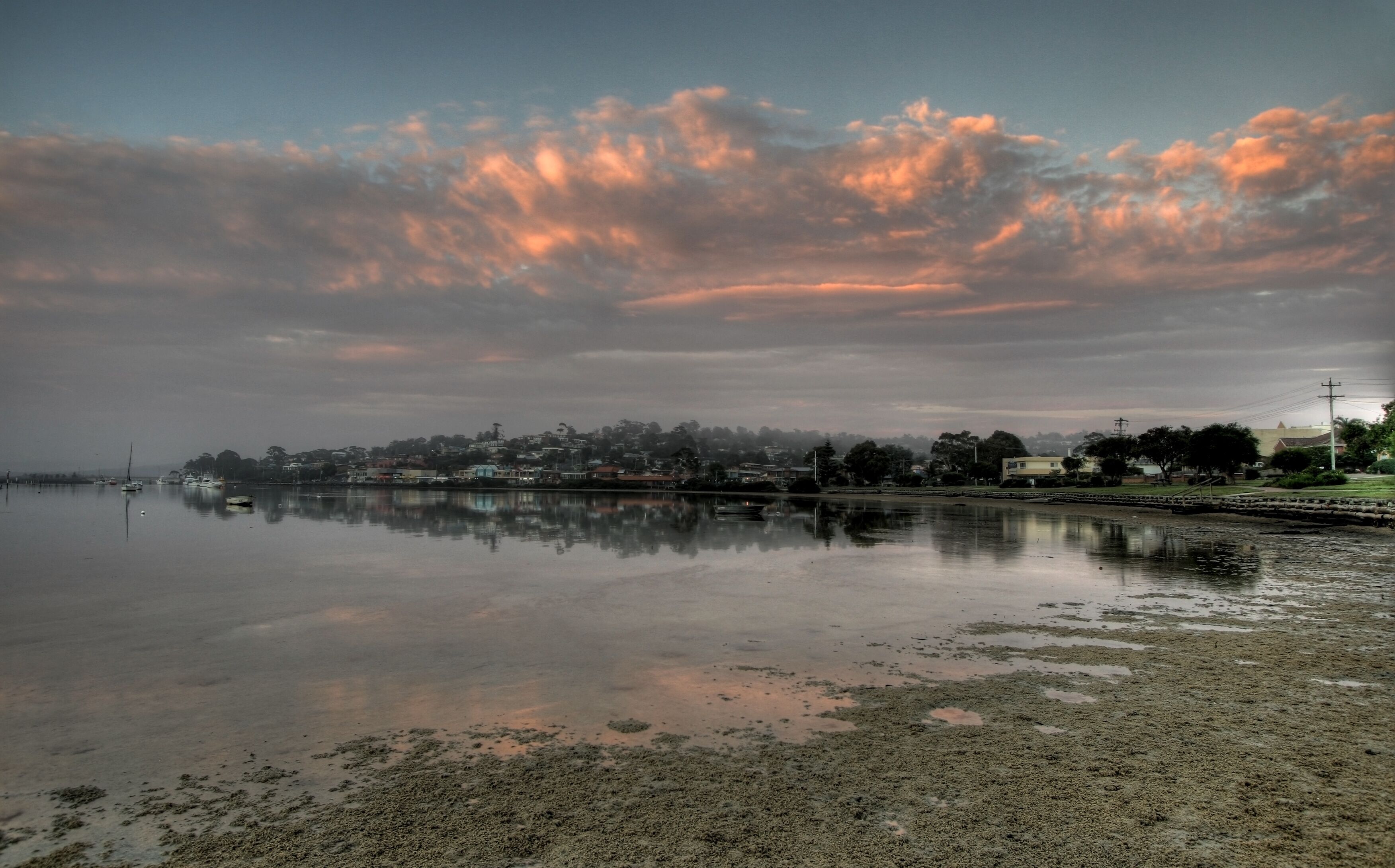 Um lago tranquilo refletindo o céu, rodeado por uma cidade com casas e árvores.