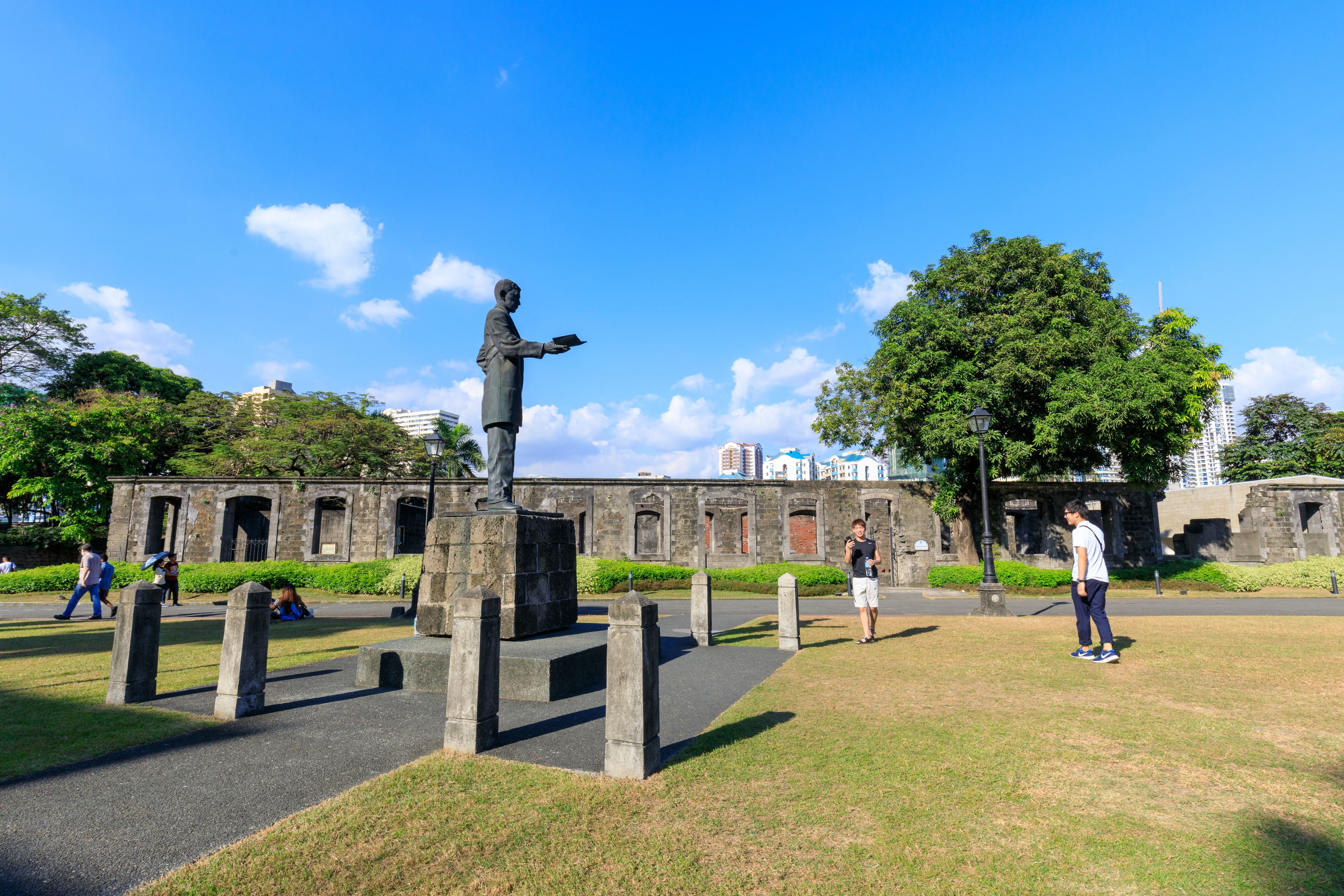 Uma estátua em um parque, com um edifício de pedra ao fundo.