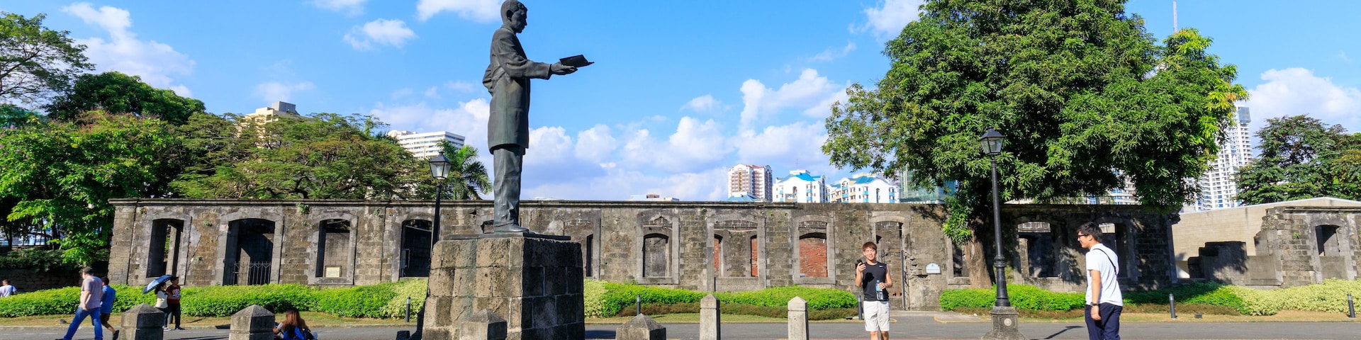Uma estátua em um parque, com um edifício de pedra ao fundo.