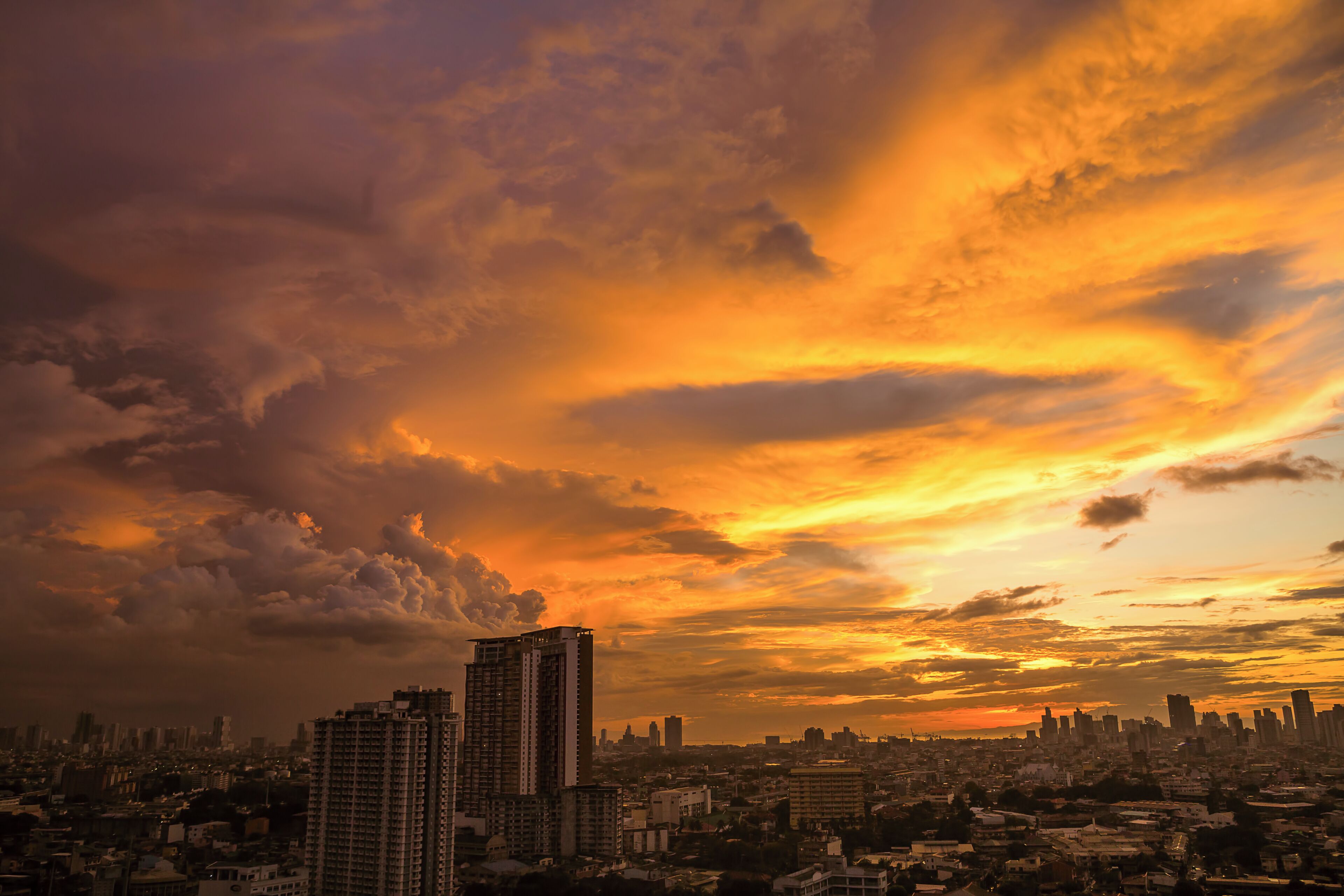 Silhueta urbana ao pôr do sol, com nuvens alaranjadas e marcantes.