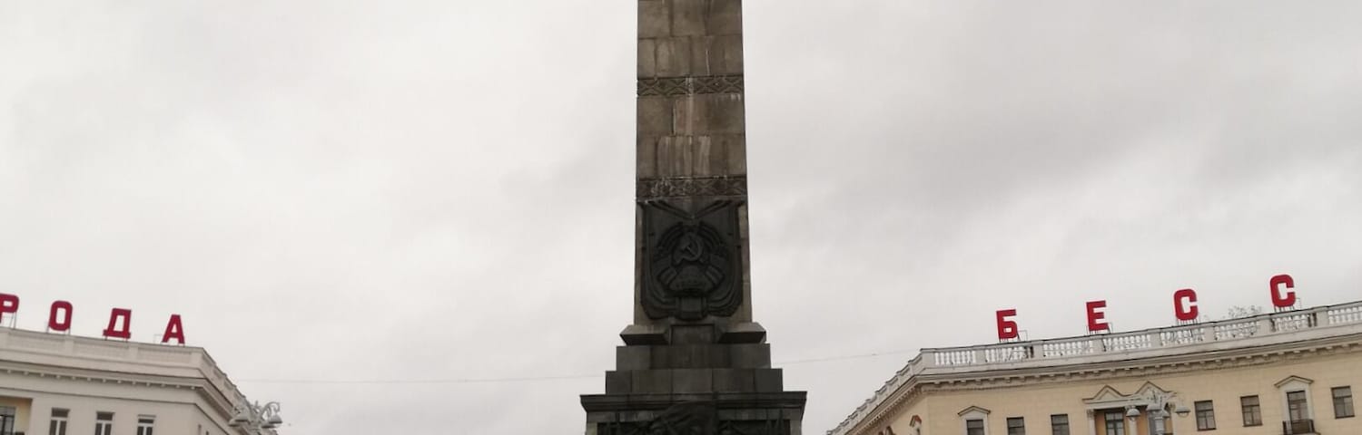 Um monumento alto com uma estrela no topo, cercado por edifícios com letras vermelhas.