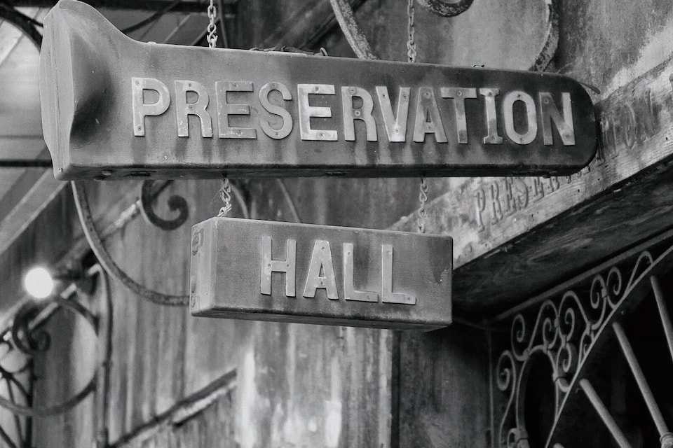 Uma placa com a inscrição 'PRESERVATION HALL' pendurada em uma estrutura metálica.