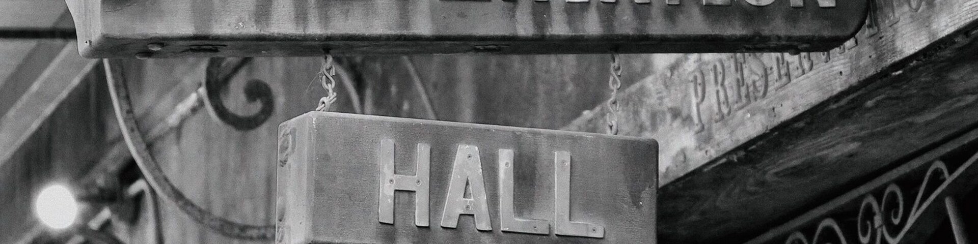 Uma placa com a inscrição 'PRESERVATION HALL' pendurada em uma estrutura metálica.