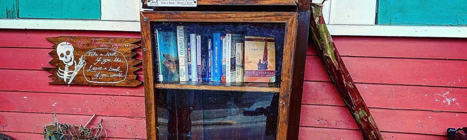 Uma estante com livros, um esqueleto e um relógio em um edifício vermelho.