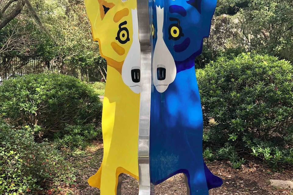 Escultura de dois animais estilizados, um amarelo e um azul, sobre um pedestal em um parque.