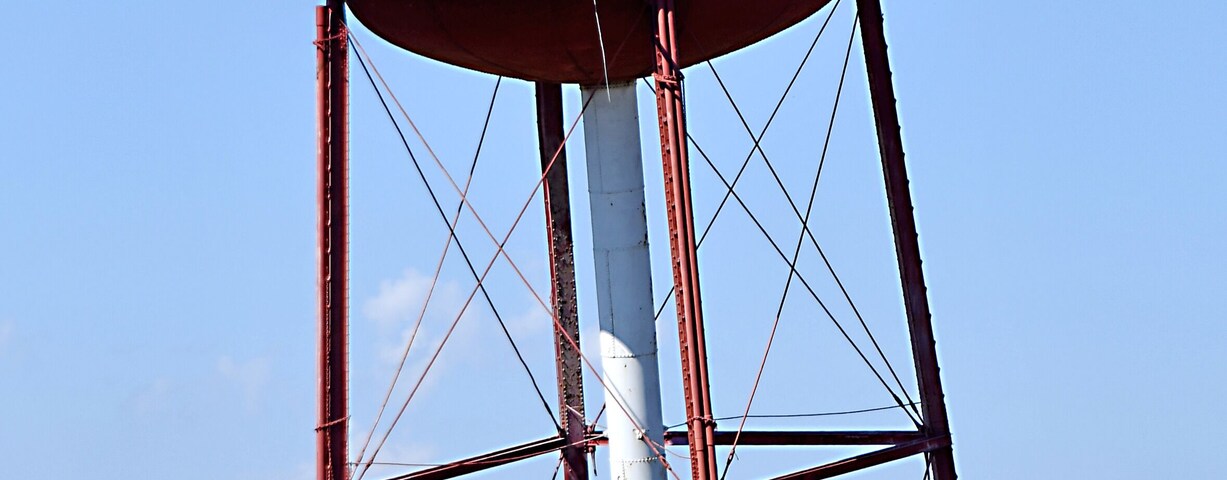 This water tower slanted at an uncomfortable angle off the old Route 66 was an ingenious marketing ploy.
Despite a population of 574 residents and its location in the middle of nowhere, the town of Groom, Texas has nearly as many unique attributes as it does people.
These include a small stretch of the original Route 66, the site of the plot of Cross Canadian Ragweed’s song “42 miles,” the seventh-largest freestanding cross in the world (at 190 feet), and a strange leaning water tower slanted at an uncomfortable angle.
This water tower lies right alongside the former path of Route 66, which has since been paved over to create US Interstate 40. During the early and mid 20th century, passersby on the Mother Road were intrigued by the severe tilt of the tower, asking themselves what on Earth could have caused it. A crashing plane? An earthquake? A giant tornado?
In reality, it was the work of a heavy-duty vehicle and a bulldozer. Ralph Britten, a man who wanted to start up a truck stop and restaurant off Route 66 in Groom, bought the water tower from the town of Lefors as an ingenious marketing technique to attract new visitors. He towed the enormous thing 34 miles to Groom, wrote “Britten USA” on top, and then, using a bulldozer, elevated two of its legs off the ground, dangling them in midair without support, so that the water tower made an 80 degree angle with the ground.
This helped his business immeasurably. It would catch the eye of every passing motorist on the route for years, many of them becoming terrified that the tower was in the process of collapsing. This played right into Britten’s hand. Worried route-takers often swerved off the road and into his truck stop, shouting “watch out! That tower’s about to fall!” Britten responded that it had been like that for years, and then asked them to sit down and buy food and a drink.
Britten’s manipulation of the tower did, however, require sufficient knowledge of physics. If the water tower were completely empty or completely full, its center of mass would be directly in the middle of the can, making it topple when slanted. So Britten filled it only partially, so that the low level of water would place the can’s center of mass near its base, directly above the two supporting legs, keeping it aloft.
Unfortunately, after many years of success, Britten’s truck stop burned down in a devastating fire, closing down all sales. Despite this unfortunate event, the leaning water tower is still one of the most photographed oddities.
