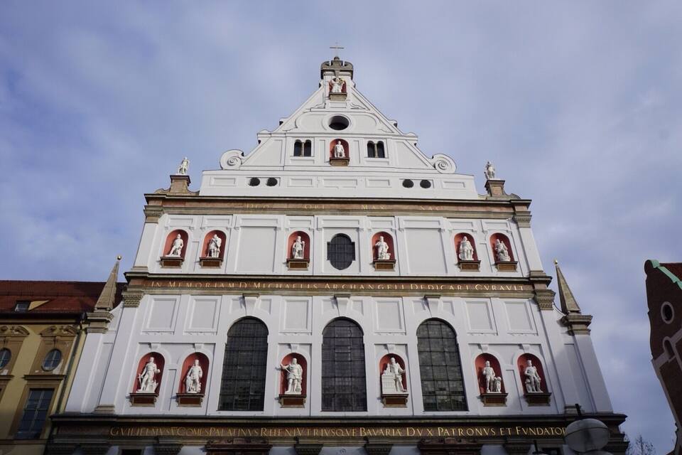 Uma igreja branca com estátuas na fachada e uma torre do relógio.