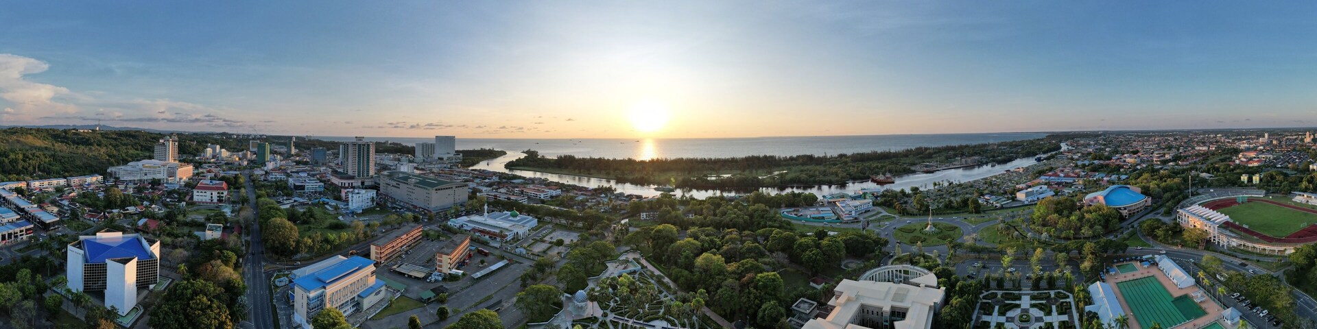 Paisagem costeira ao pôr do sol com um rio, edifícios e um parque.