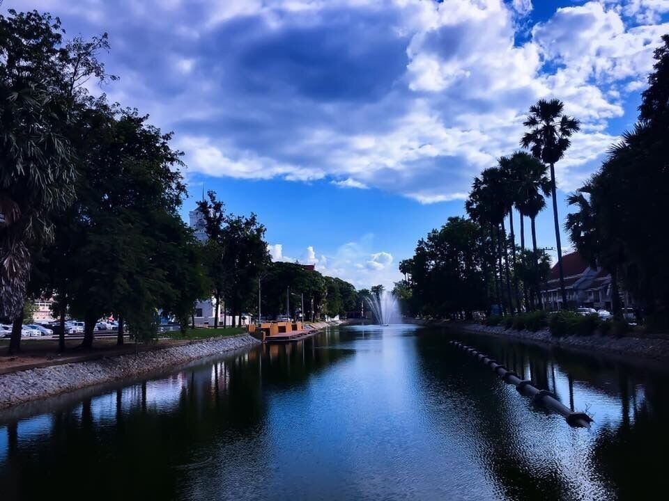 Um rio calmo com uma fonte no centro, cercado por árvores e edifícios.