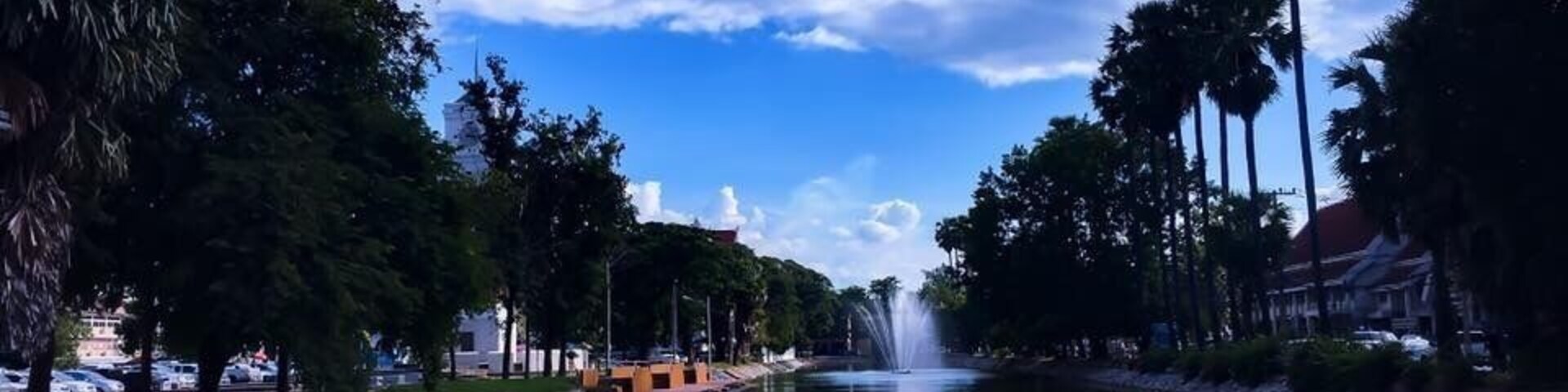 Um rio calmo com uma fonte no centro, cercado por árvores e edifícios.