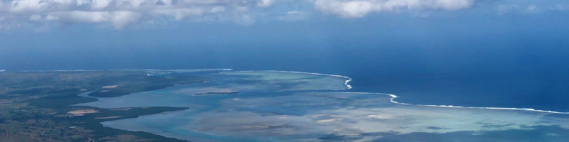 Vista aérea de uma paisagem costeira, com áreas verdes e águas azuis, incluindo uma praia arenosa e águas cristalinas.