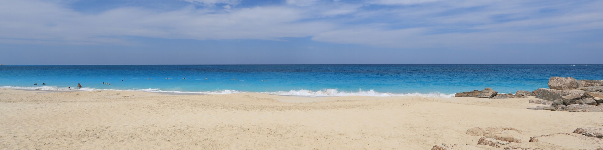 Uma praia de areia com águas azul-claras e pedras espalhadas.