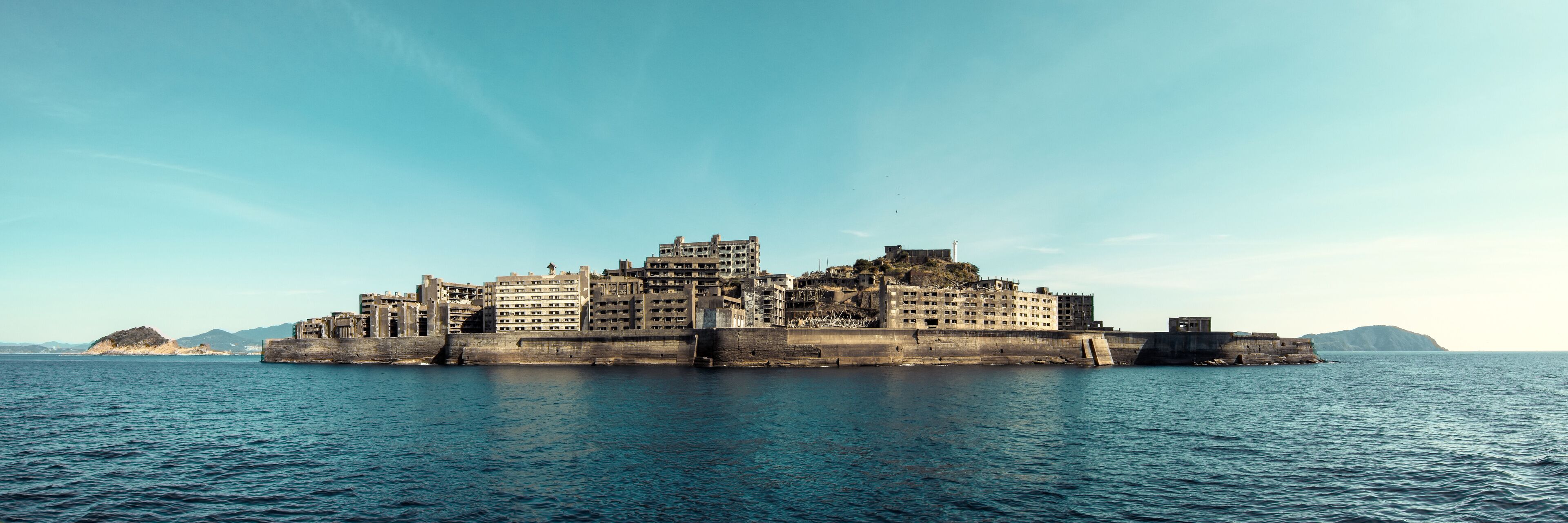 Uma fortaleza costeira com vários edifícios, uma grande massa de água em primeiro plano e ilhas ao longe.