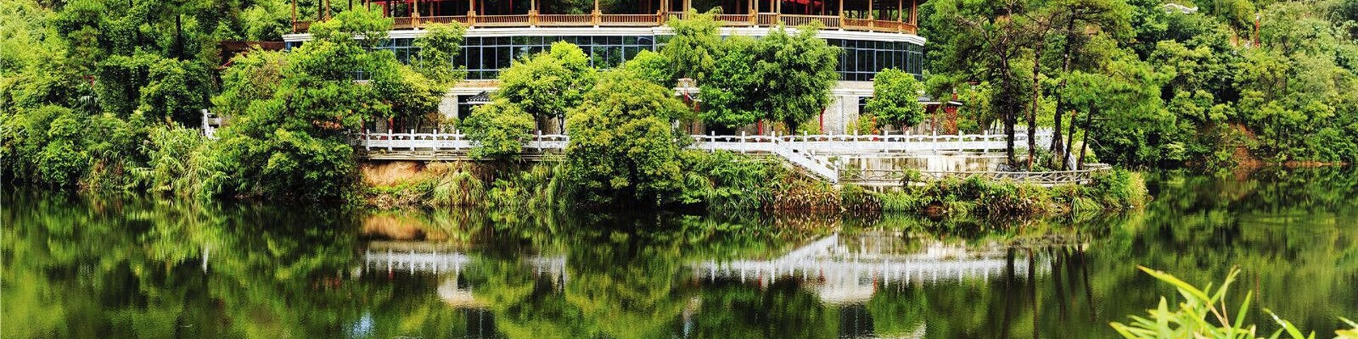 Um edifício de madeira tradicional com telhado de telhas, rodeado por vegetação exuberante e um lago tranquilo.