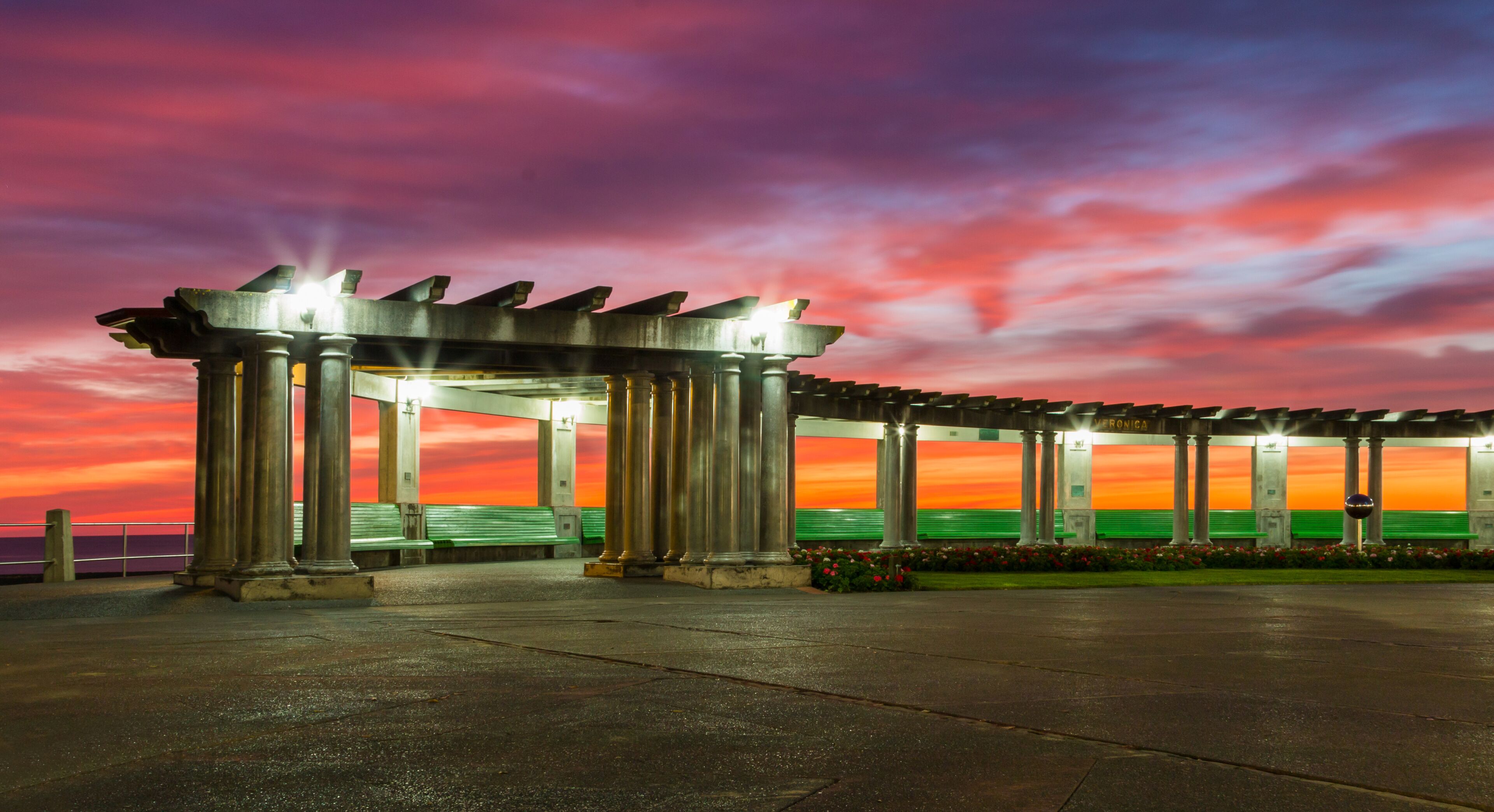 Uma galeria coberta com colunas e um pôr do sol ao fundo.