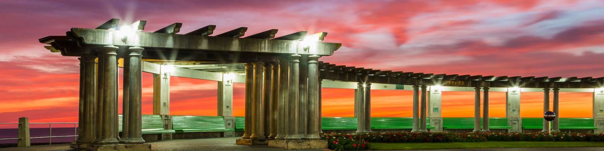 Uma galeria coberta com colunas e um pôr do sol ao fundo.