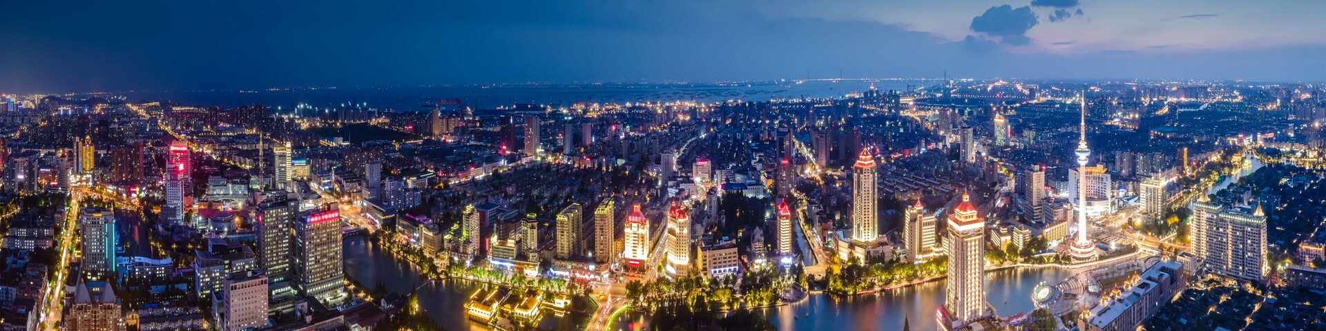 Uma paisagem urbana noturna com rio, edifícios iluminados e uma torre imponente.