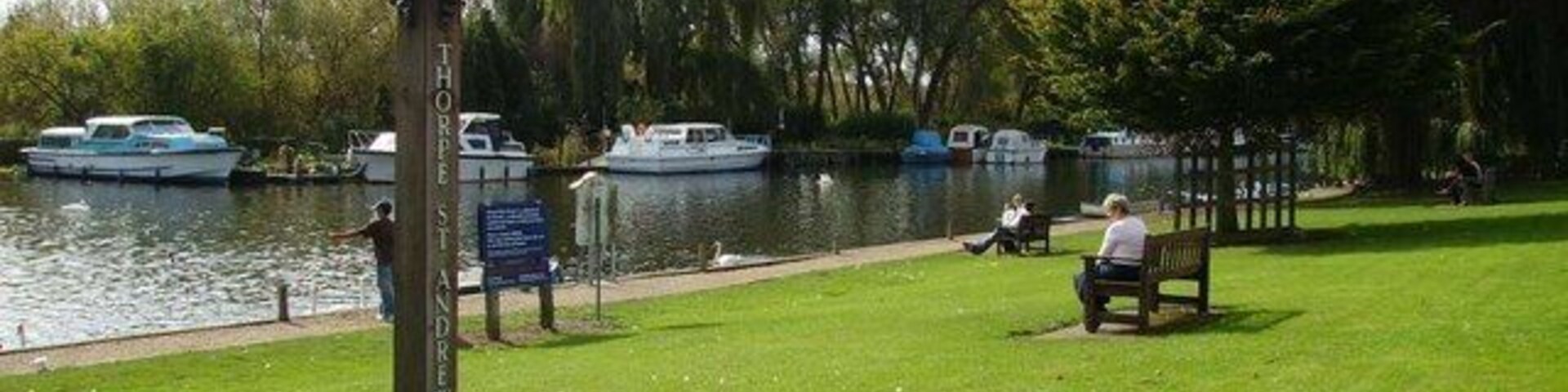 Uma estátua em um pedestal num parque, com um rio e barcos ao fundo.