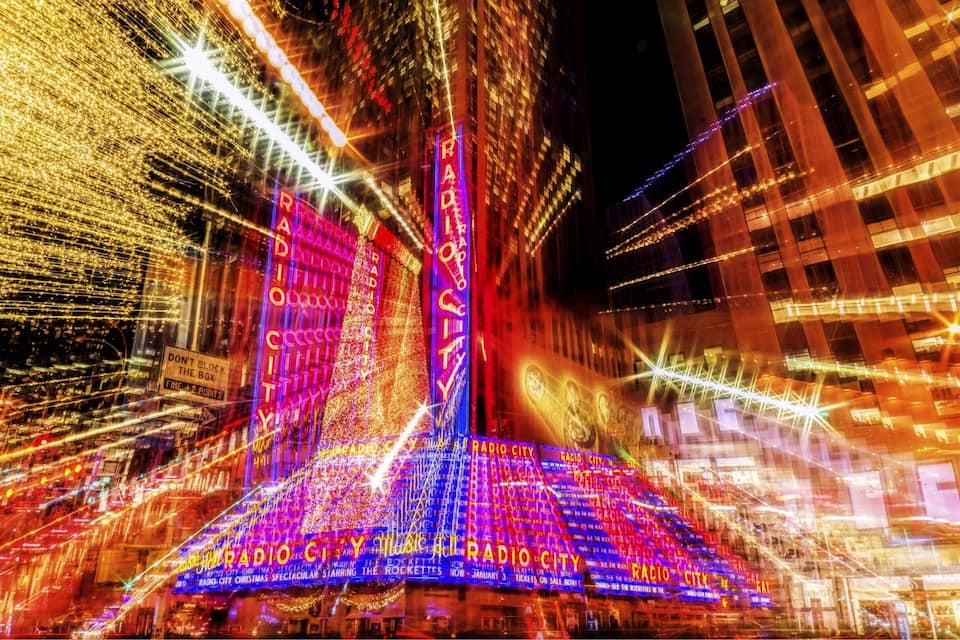 A brightly lit building with neon signs and lights, including "Radio City Music Hall" and "Radio City Music Hall Christmas Spectacular."