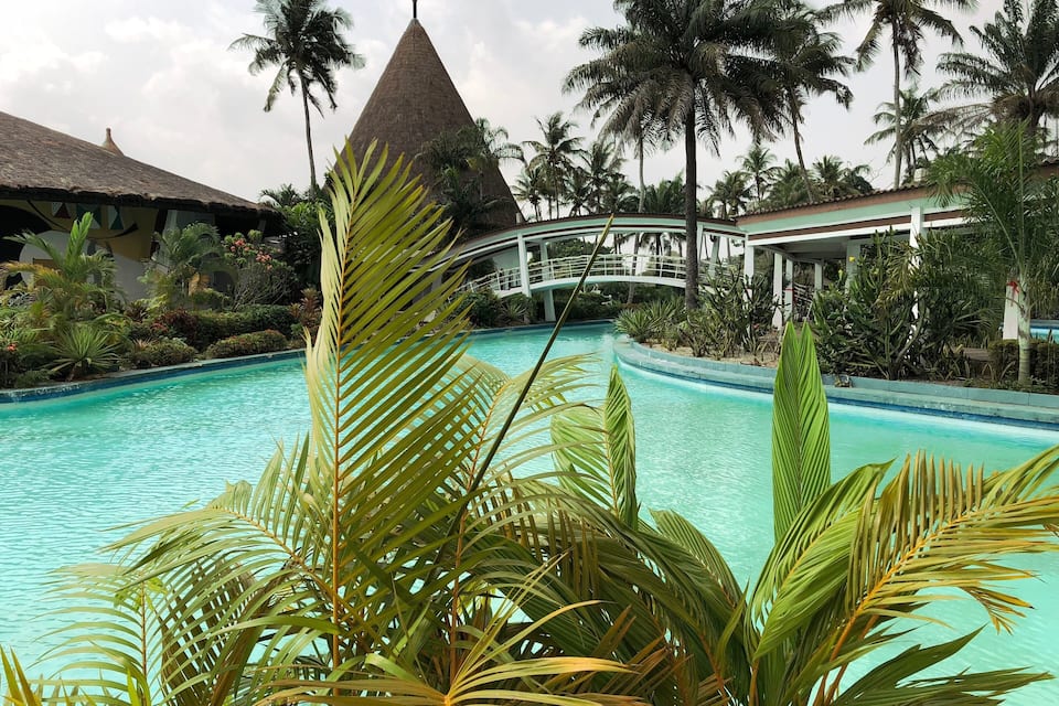 Piscina cercada por palmeiras e um edifício com telhado de palha.