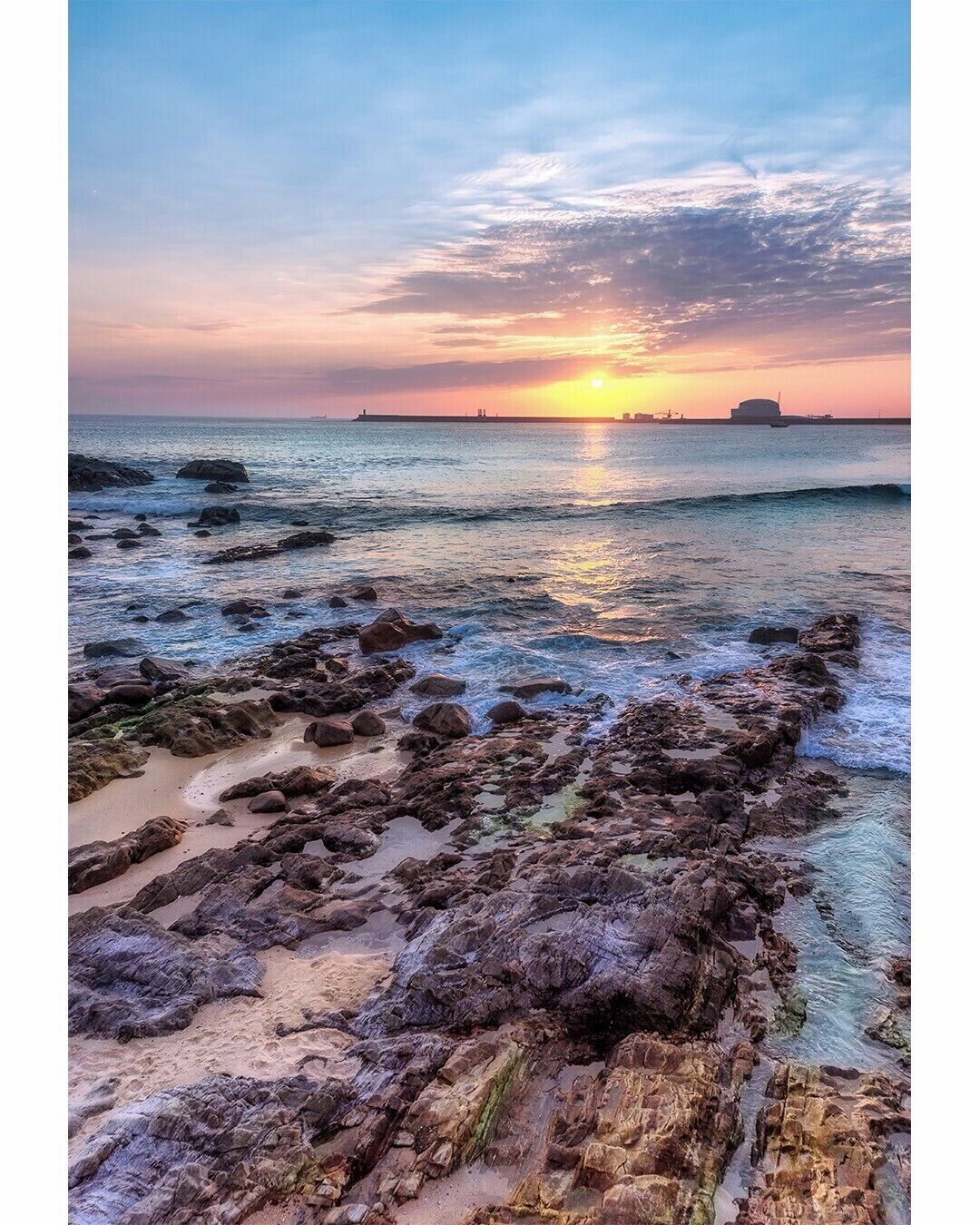 Uma costa rochosa com ondas ao pôr do sol.