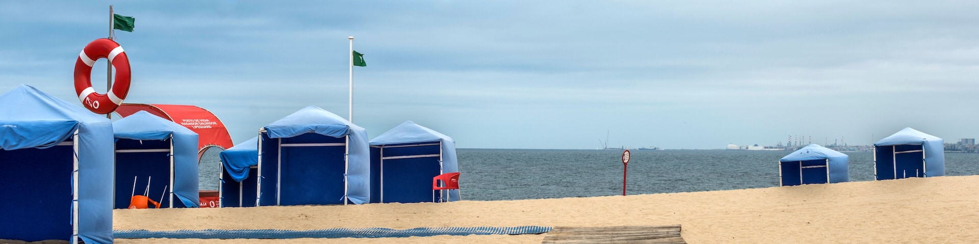 Uma praia com tendas azuis, um boi de salvamento e um deck de madeira.