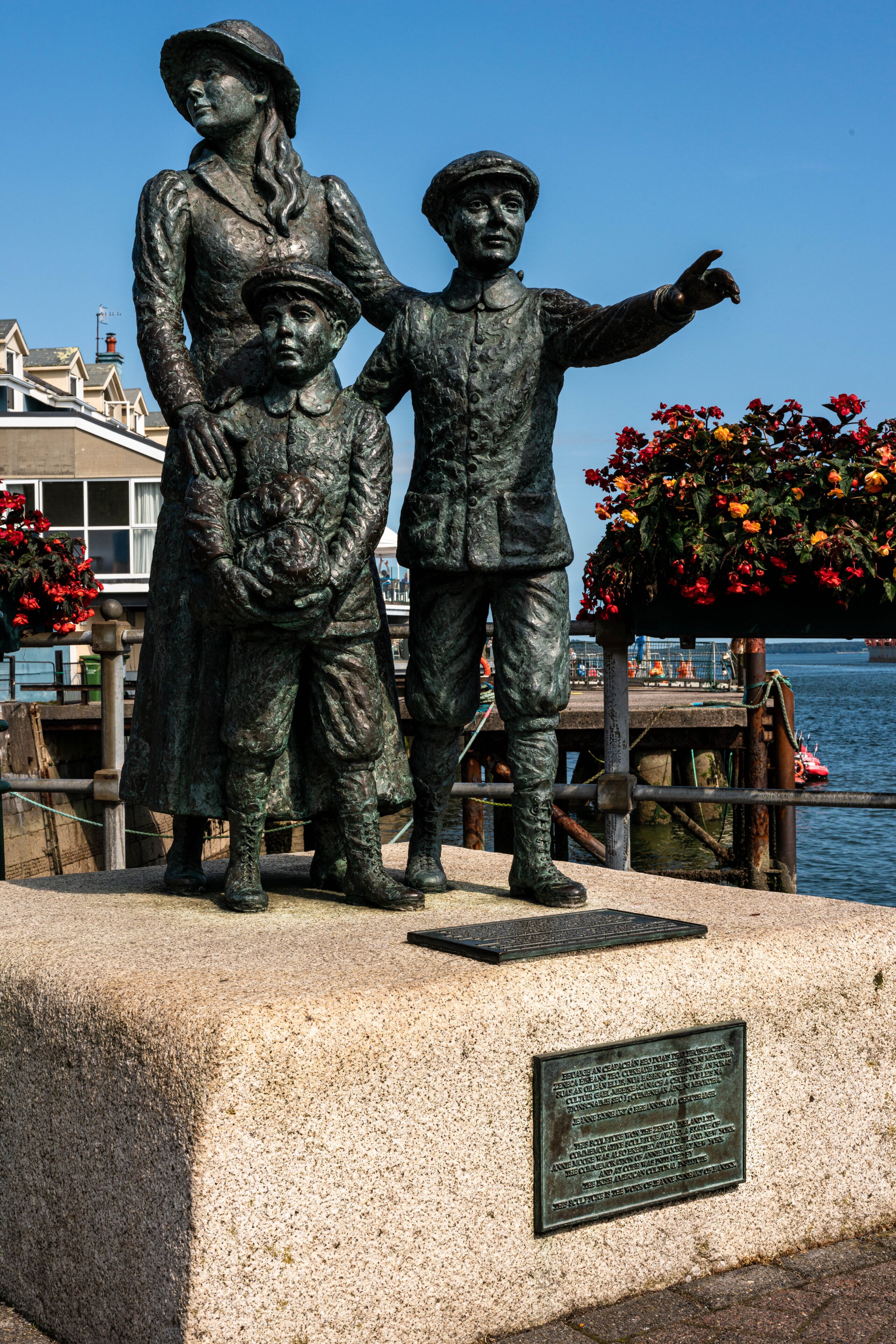 Estátua de uma mulher e duas crianças junto a uma orla marítima.