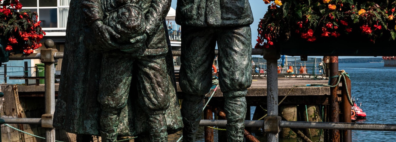 Estátua de uma mulher e duas crianças junto a uma orla marítima.