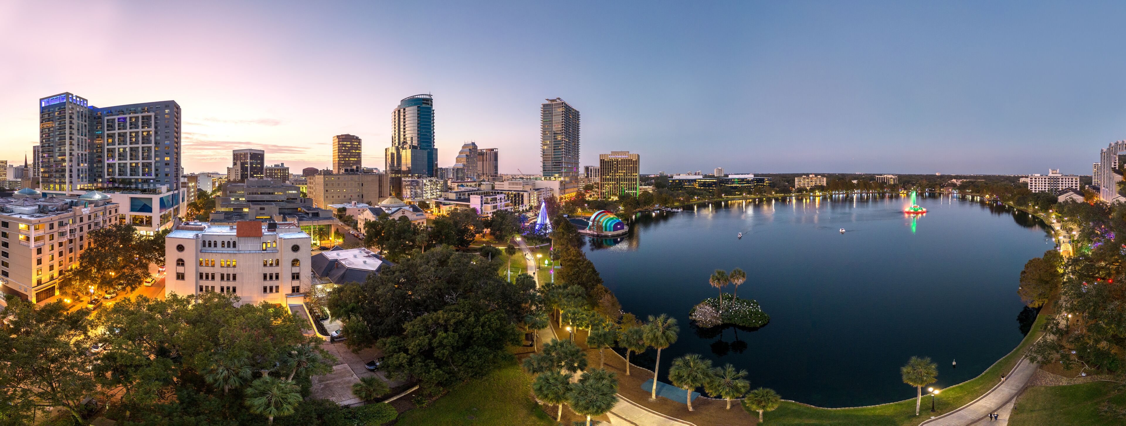 Paisagem urbana com edifícios modernos, um lago e um parque com árvores.