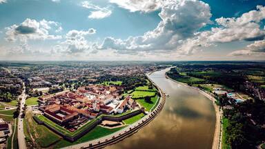 Vista aérea de uma cidade histórica com um rio, um castelo fortificado e vegetação ao redor.