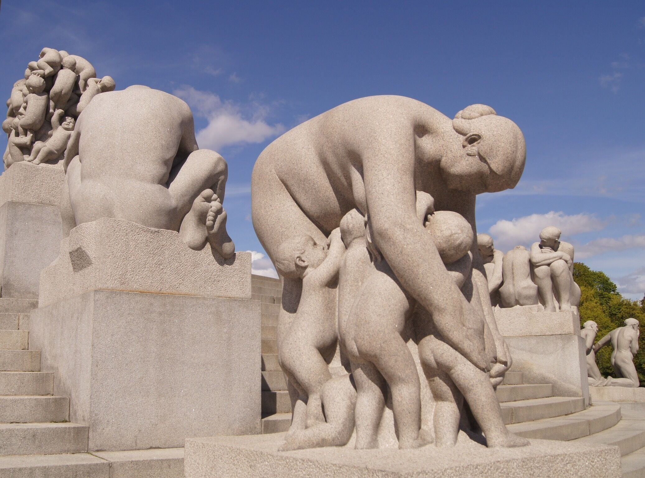 Grande escultura de pedra de uma figura nua reclinada com uma criança, apoiada em plataforma de pedra com degraus.