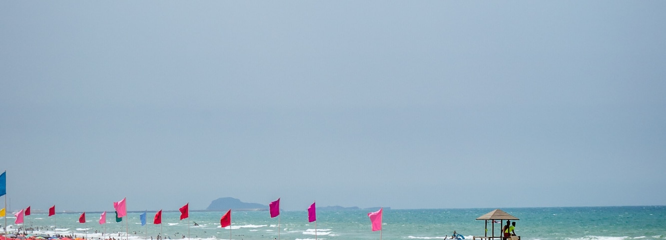 Uma praia movimentada com vários guarda-sóis coloridos e uma torre de salva-vidas.