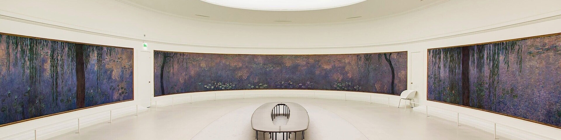 Uma galeria ampla com uma mesa central e grandes pinturas abstratas nas paredes.