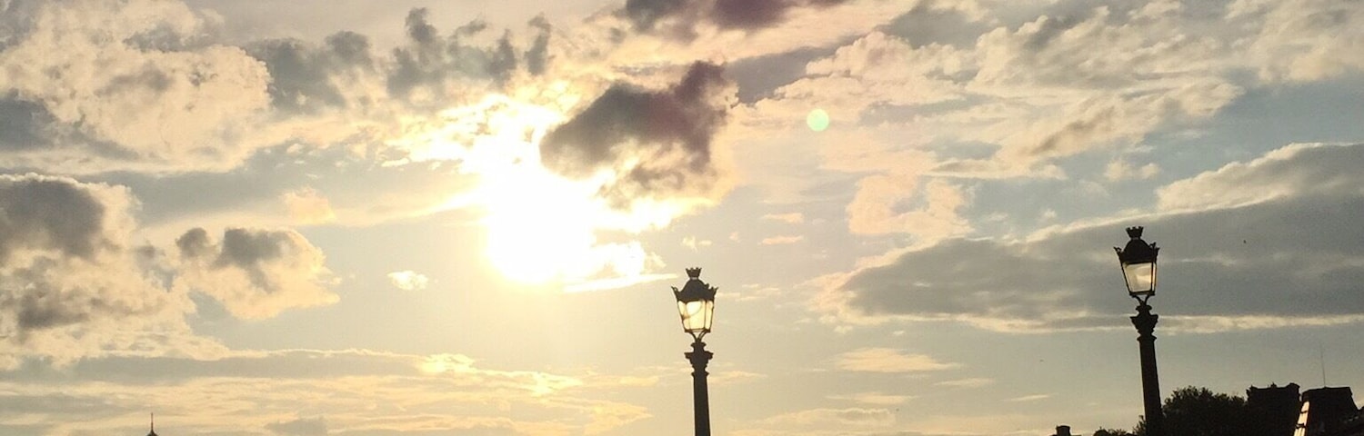 Um pôr do sol sobre uma rua de paralelepípedos, com postes de iluminação e uma torre ao fundo.