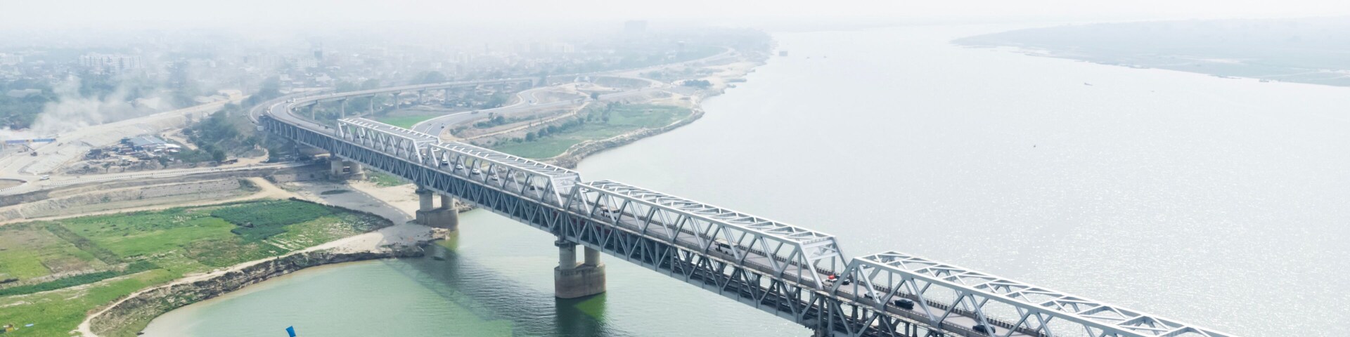 Uma grande ponte de aço que atravessa um rio, com um horizonte urbano ao fundo.